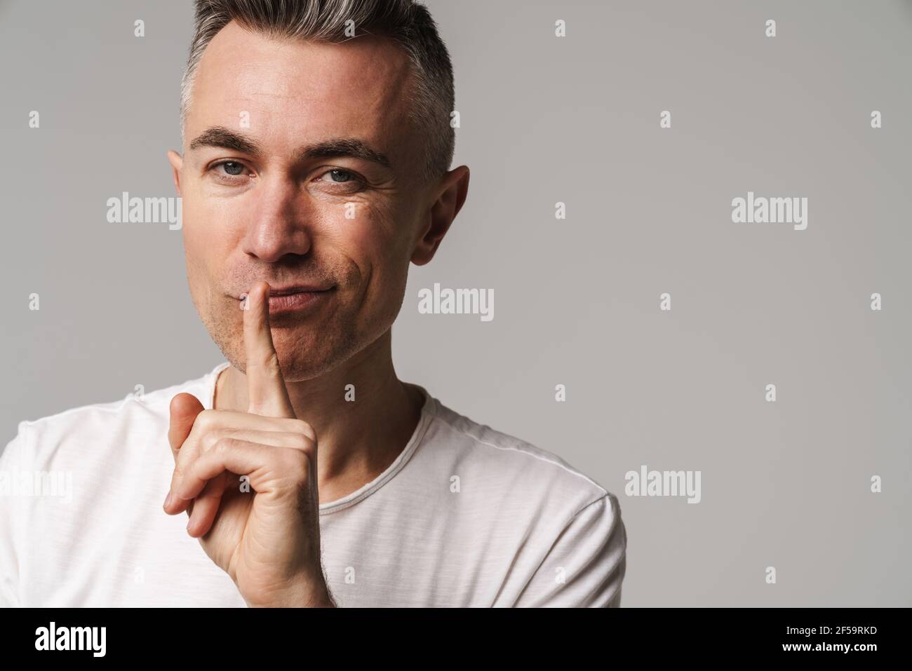 Serious man with finger on lips keeping a secret isolated over gray ...