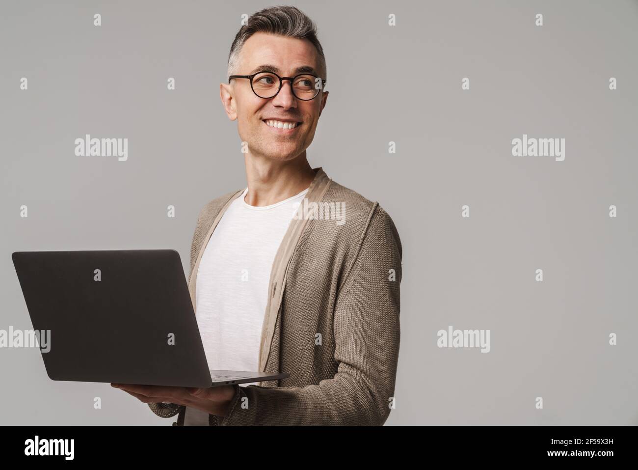 Confident smiling handsome smart looking man standing with laptop computer isolated over gray ...