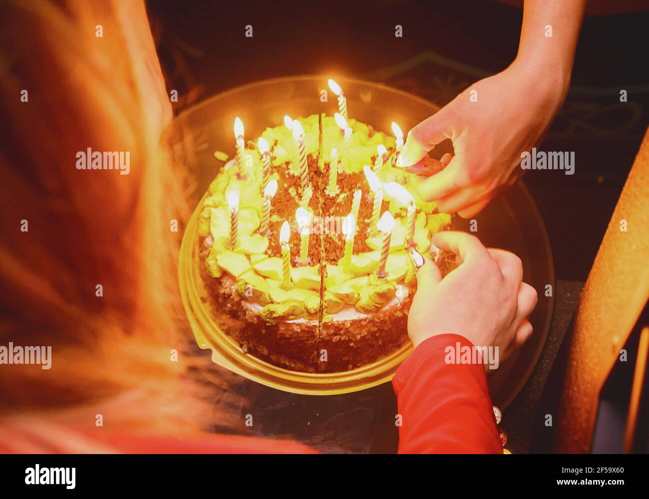 Girl's hands set fire to candles on a cake on a holiday in the dark ...