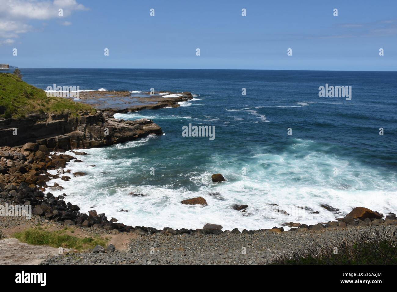 Beautiful view of the wavy ocean hitting the rocky beach under the blue ...