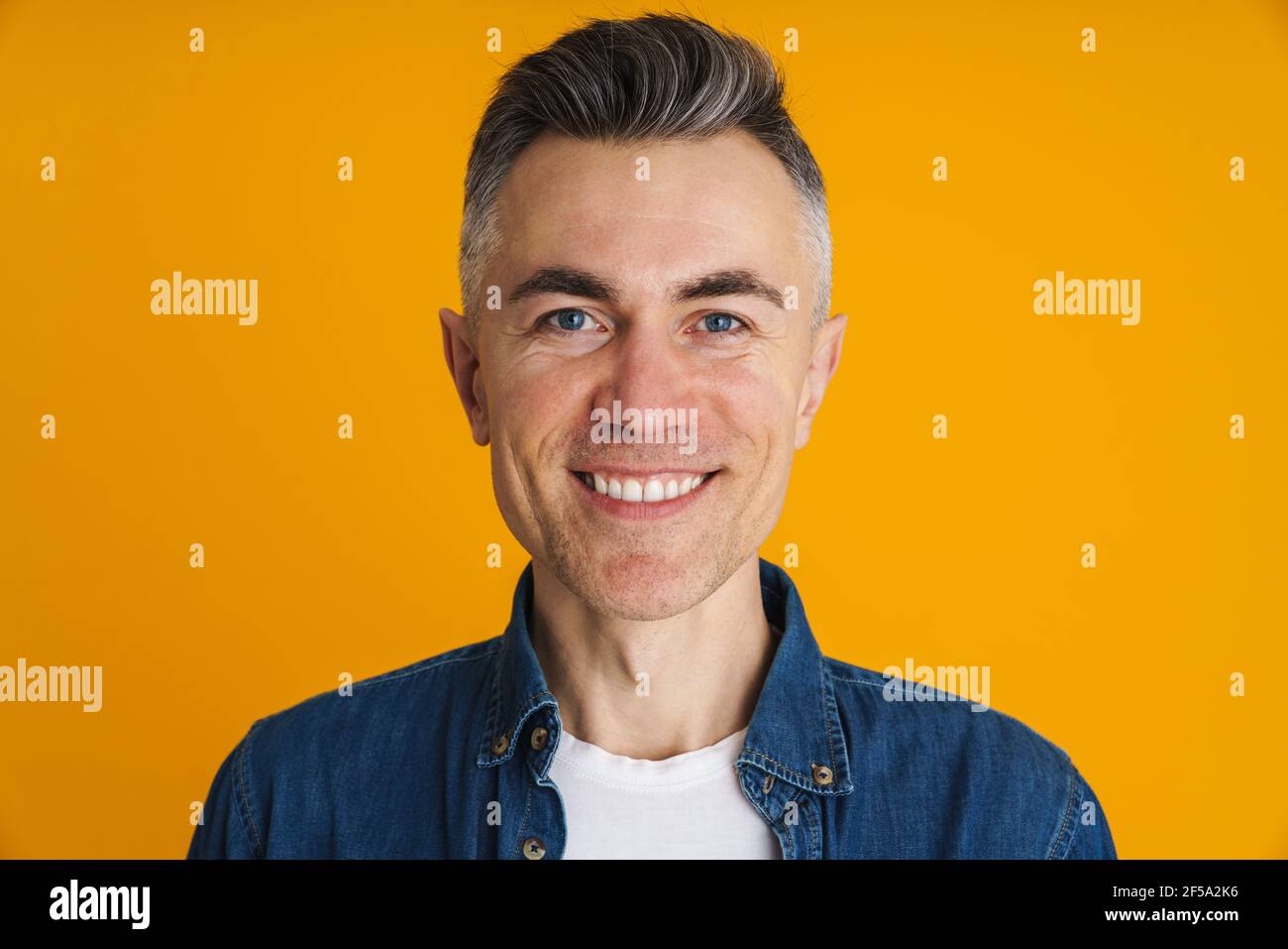 Joyful handsome man smiling and looking at camera isolated over yellow ...