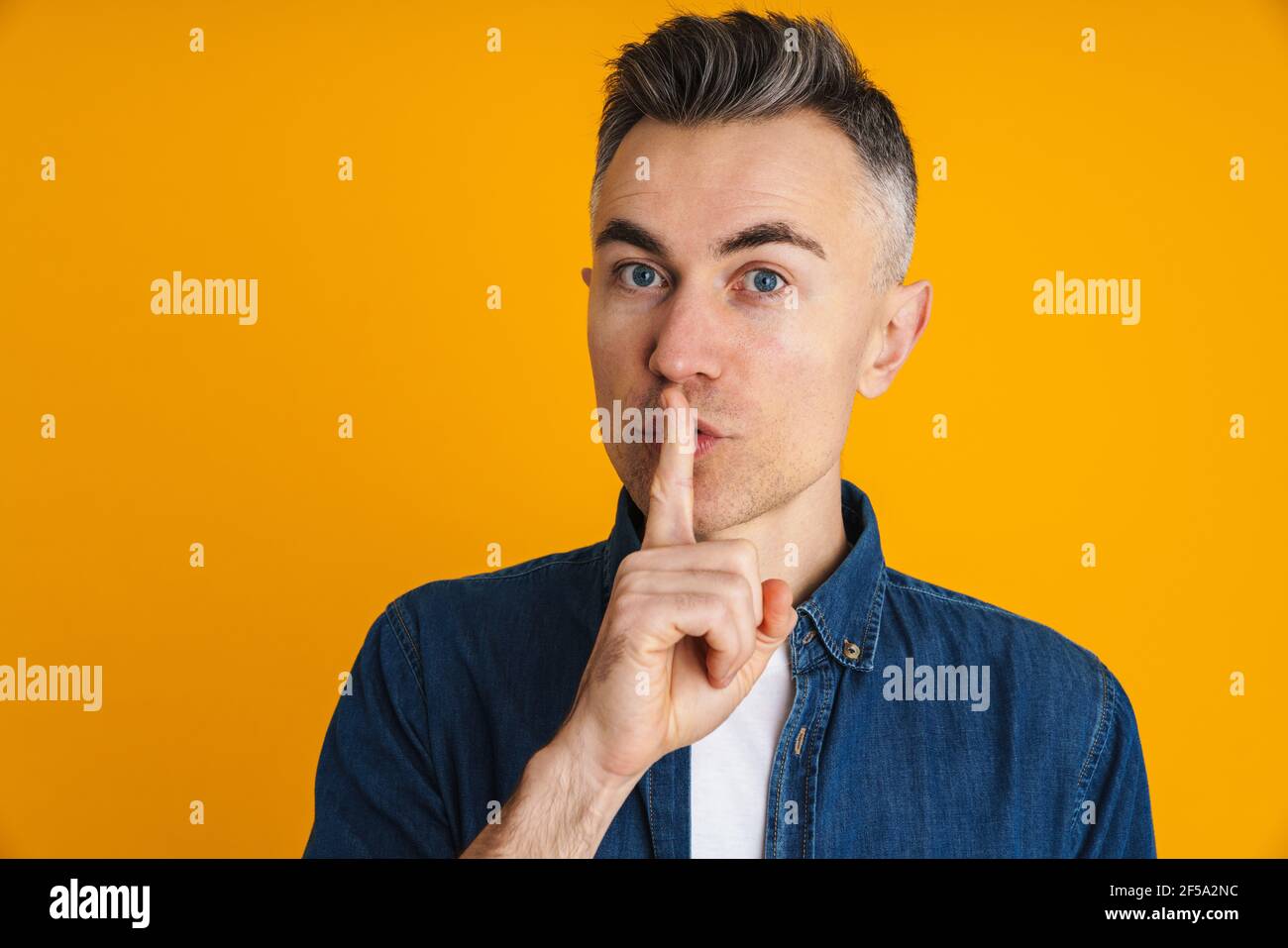 Serious handsome man showing silence gesture at camera isolated over ...