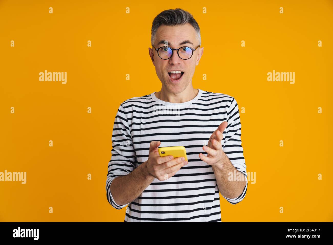 Excited handsome man exclaiming while using cellphone isolated over ...