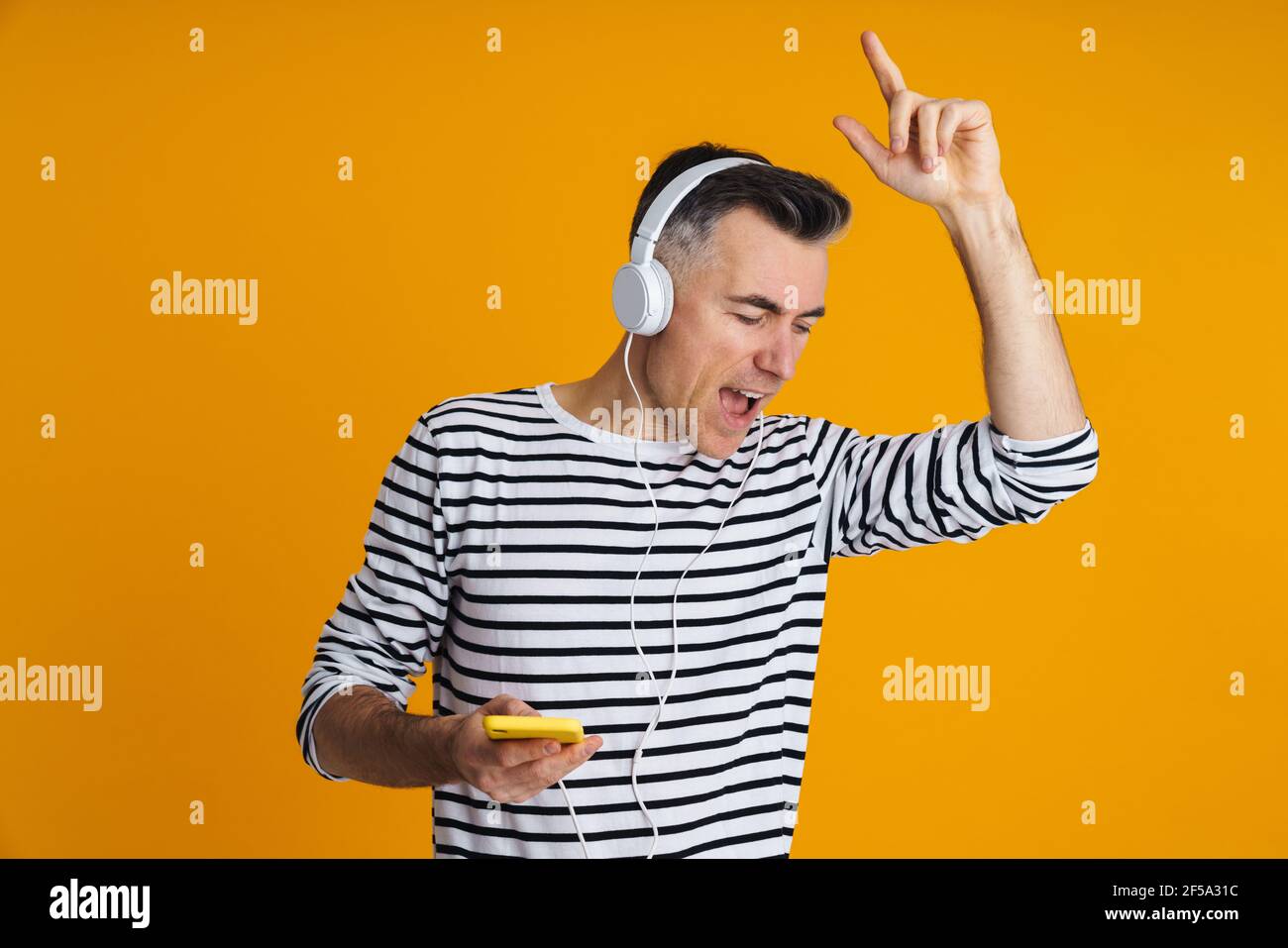 Joyful man in headphones dancing and using mobile phone isolated over ...