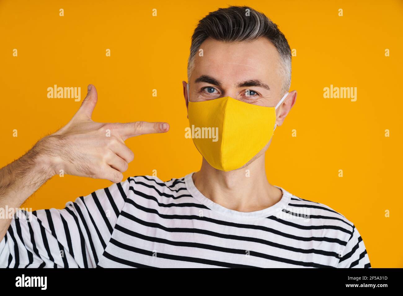 Joyful handsome man pointing at his protective mask isolated over ...