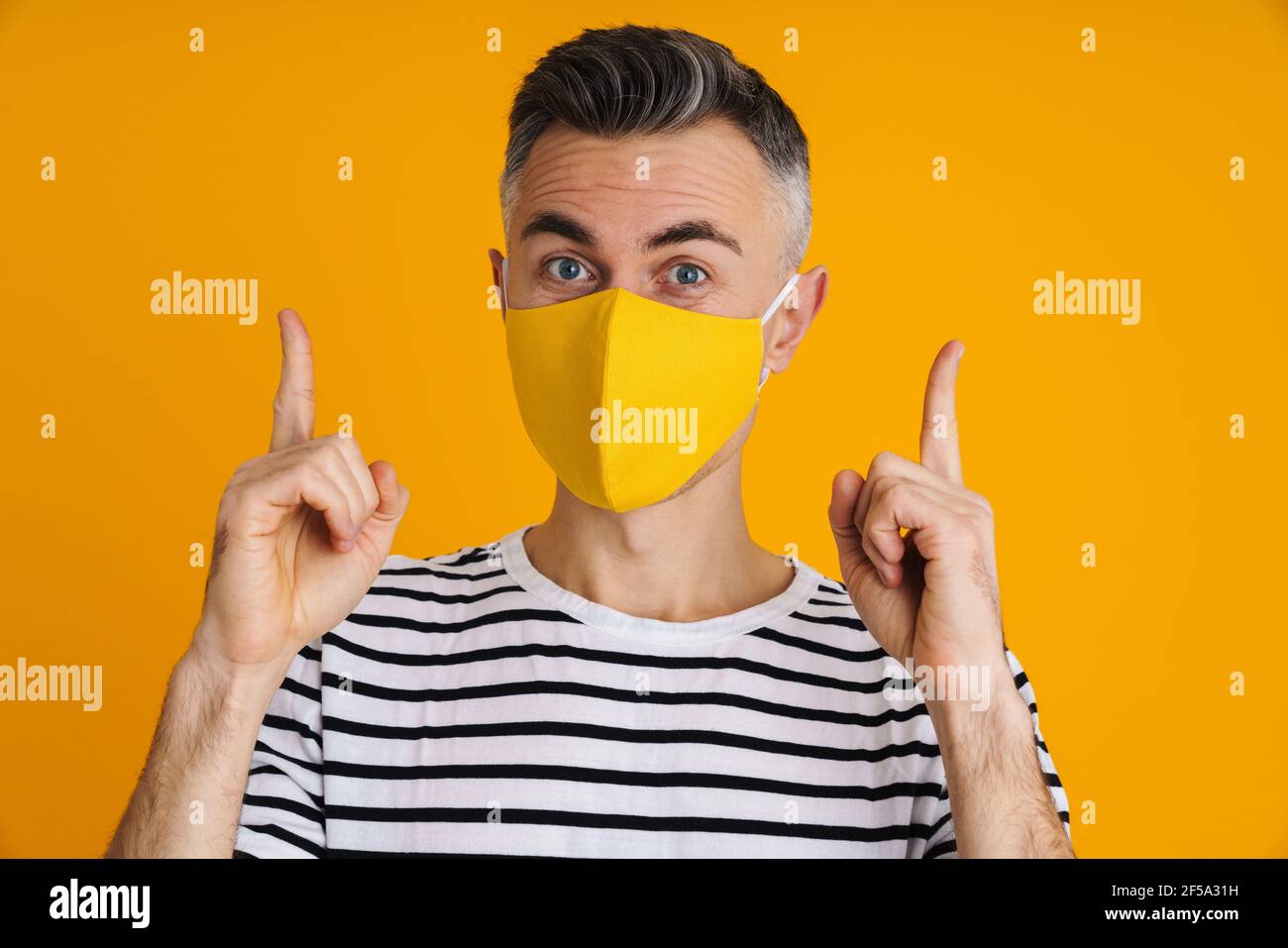 Excited handsome man in protective mask pointing fingers upward ...