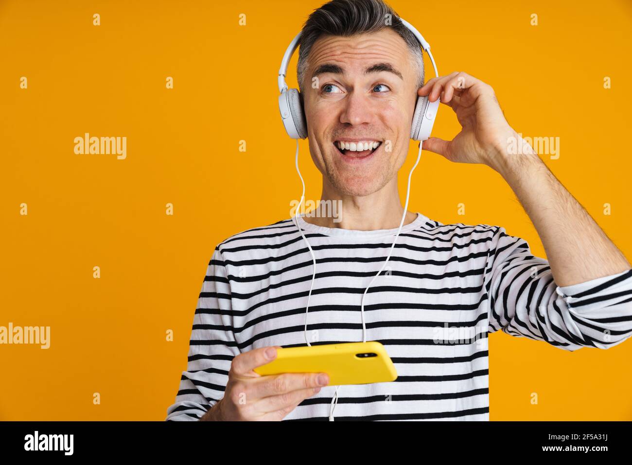 Joyful man in headphones smiling and using mobile phone isolated over ...