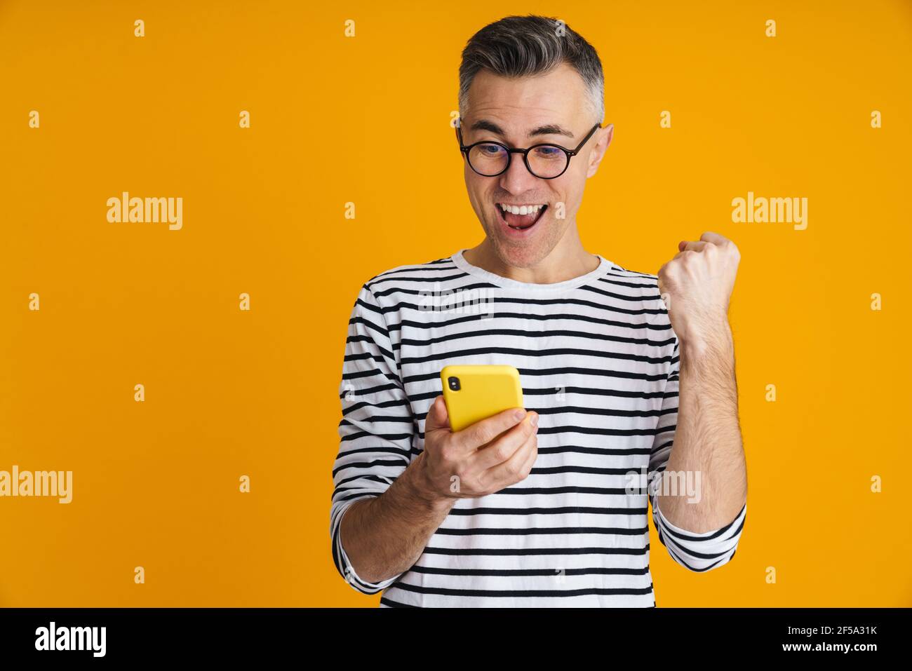 Excited handsome man making winner gesture while using cellphone ...