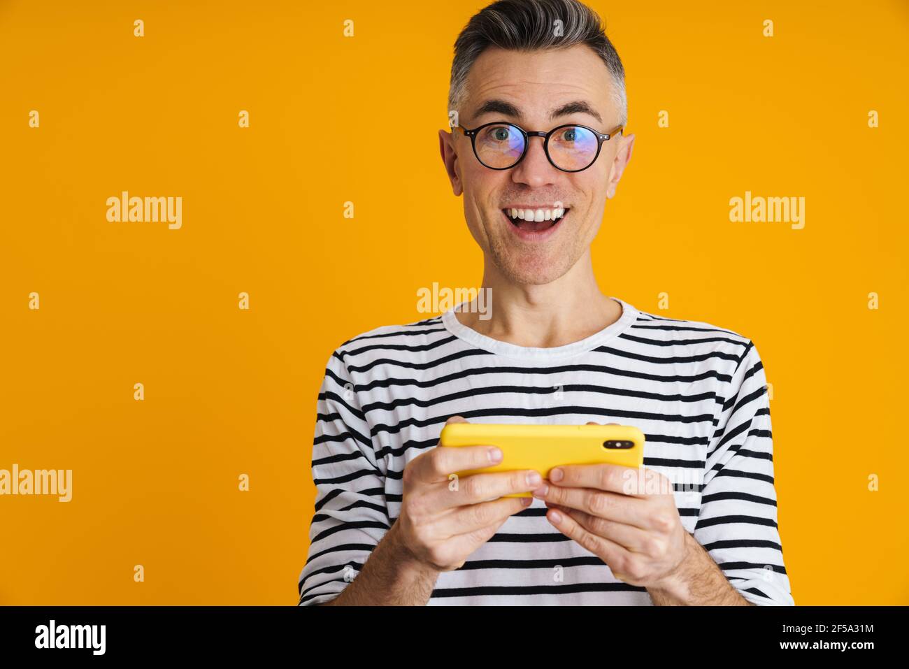 Delighted handsome man playing online game on mobile phone isolated ...