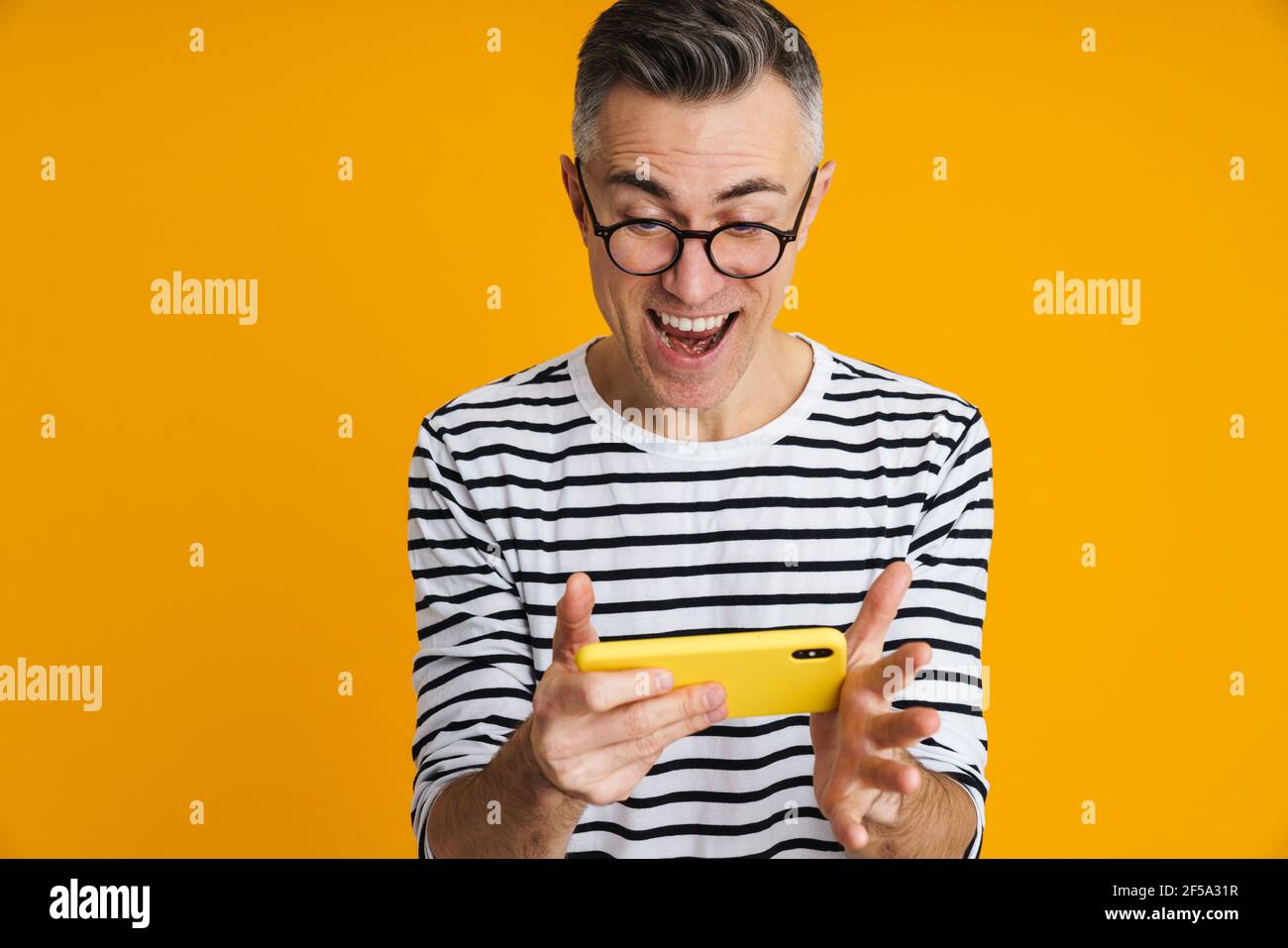 Delighted handsome man playing online game on mobile phone isolated ...