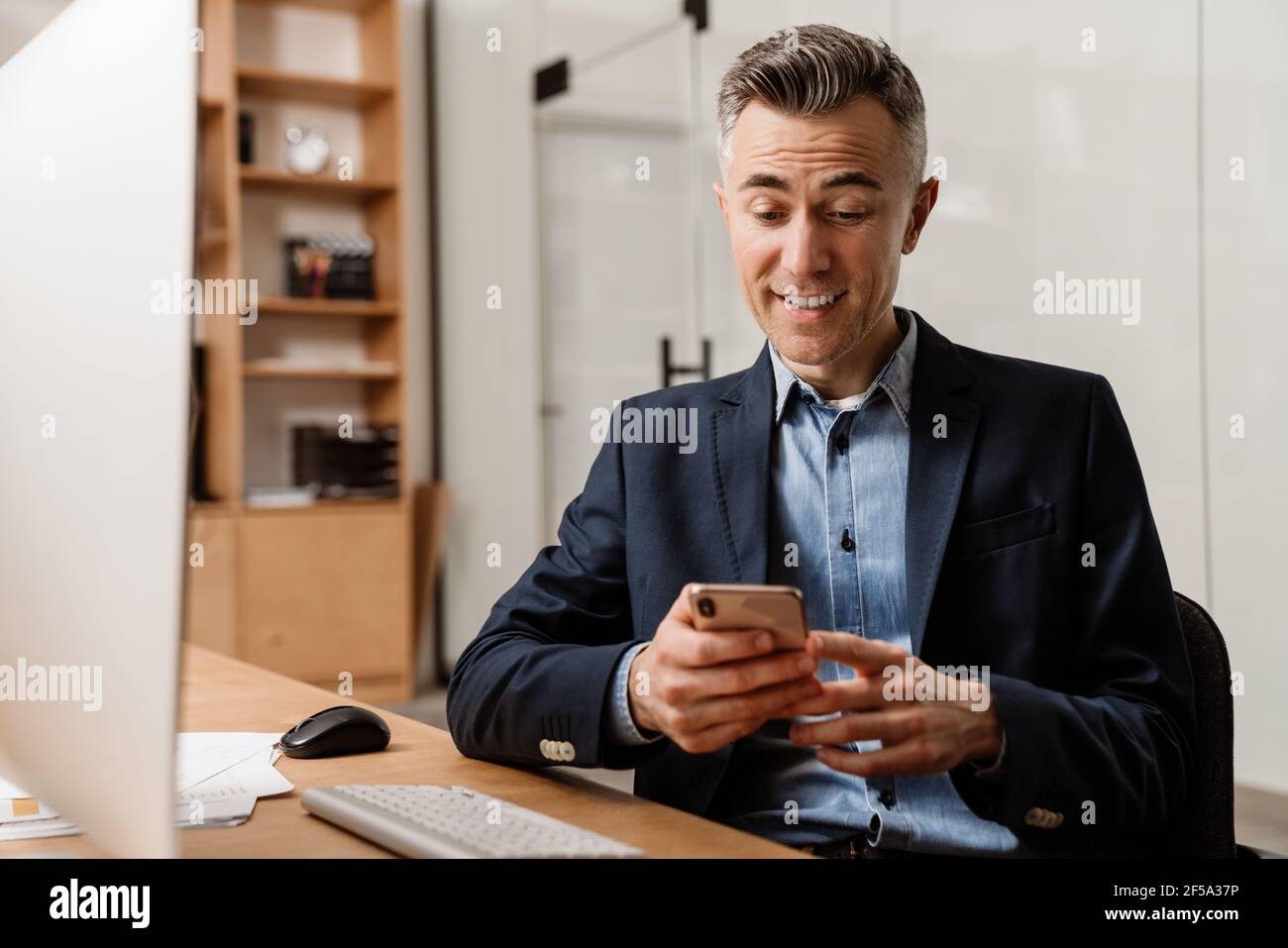 Excited grey man using mobile phone while working with computer in ...