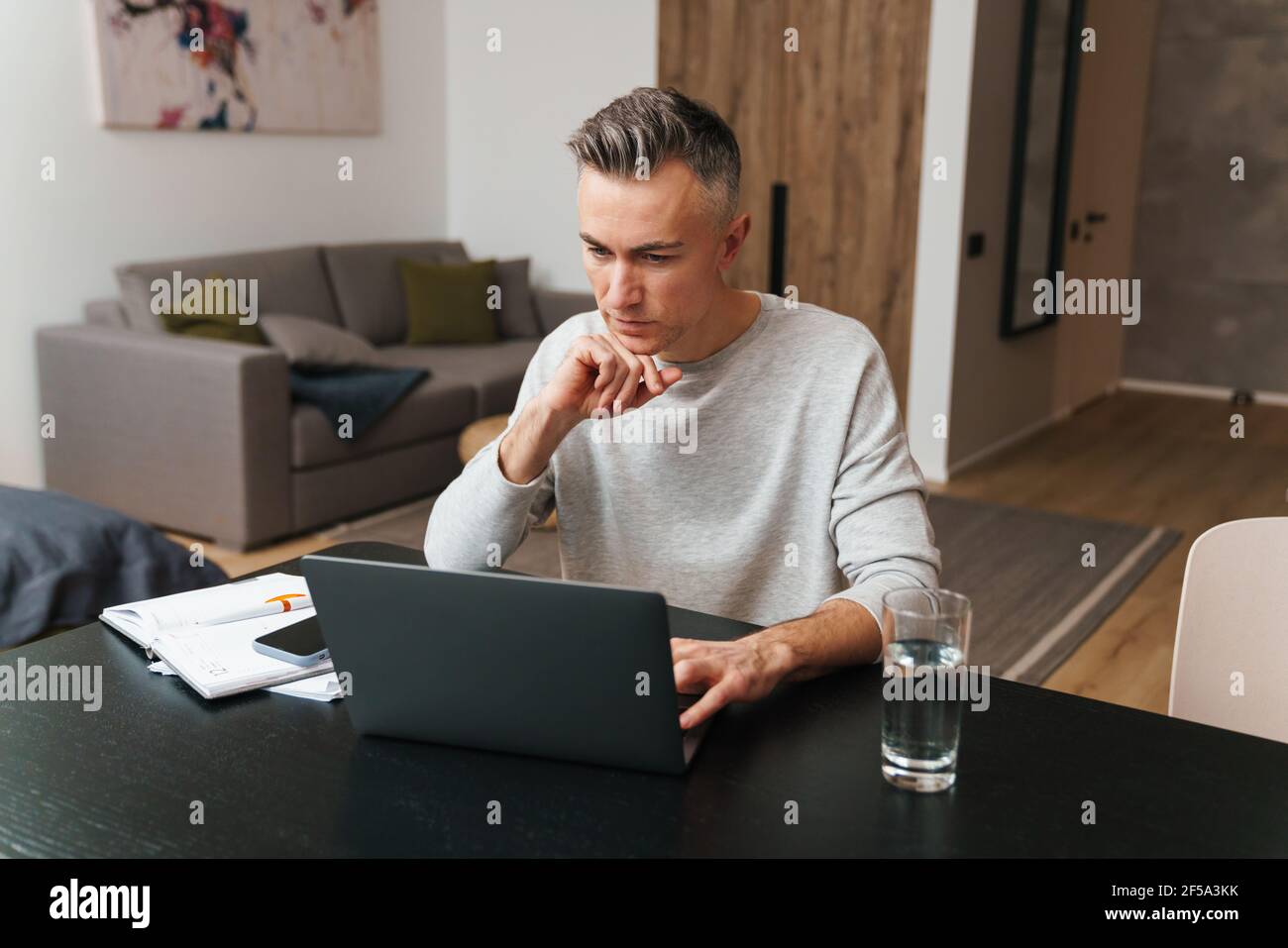 Serious grey man working with laptop while sitting in living room at ...