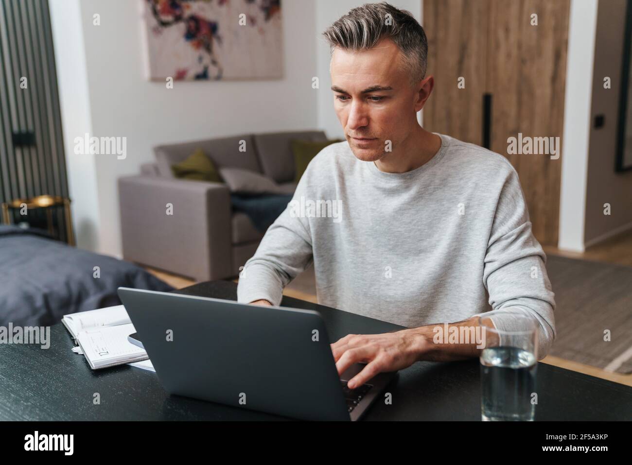 Serious grey man working with laptop while sitting in living room at ...