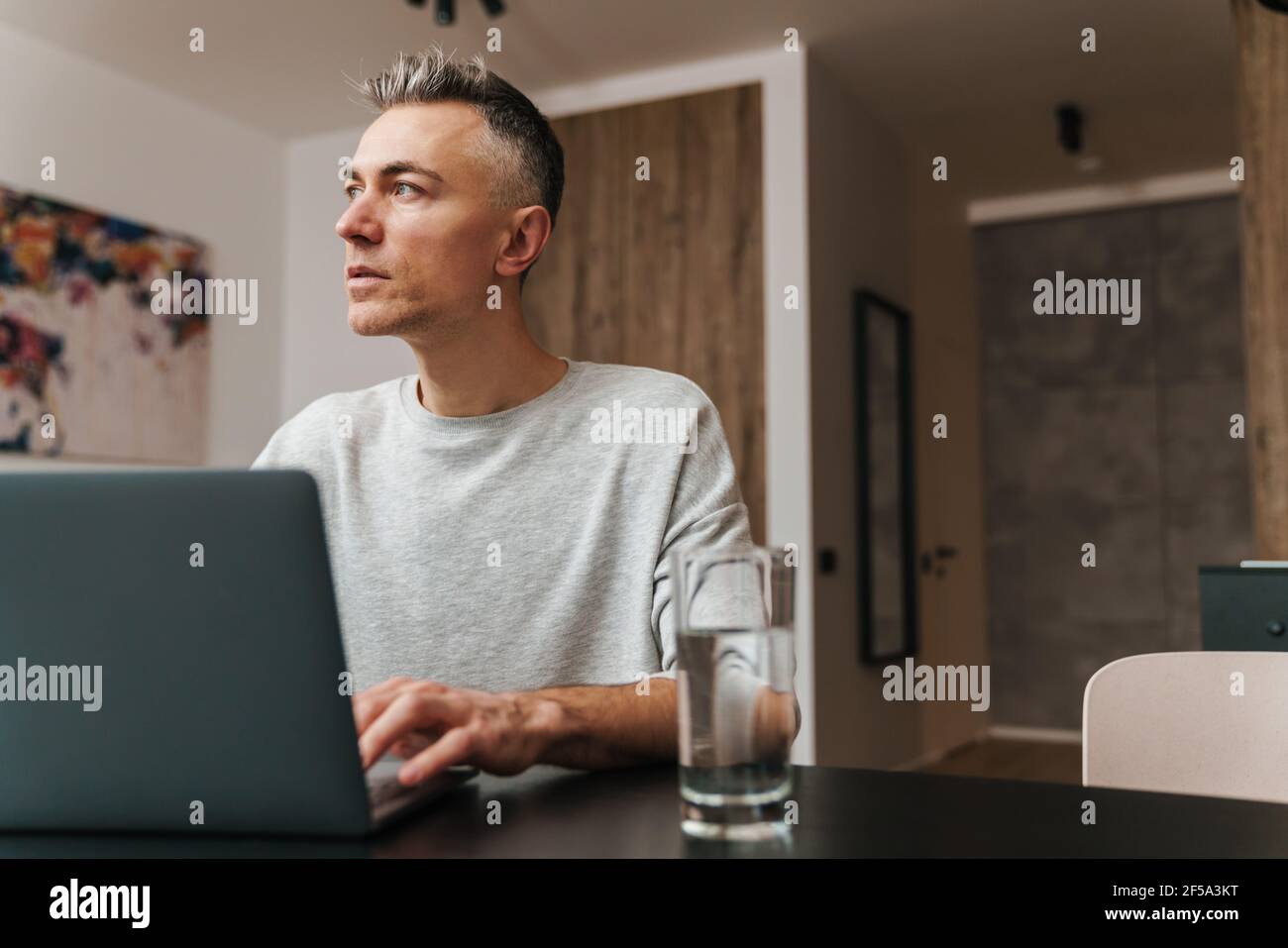 Serious grey man working with laptop while sitting in living room at ...
