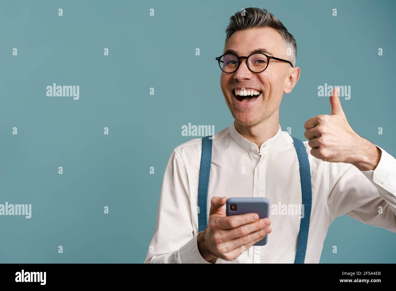 Happy grey-haired man showing thumb up and using cellphone isolated ...