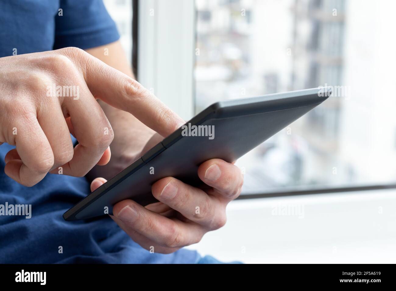 Gray e-reader electronic book in male hands. A man in a blue t-shirt ...