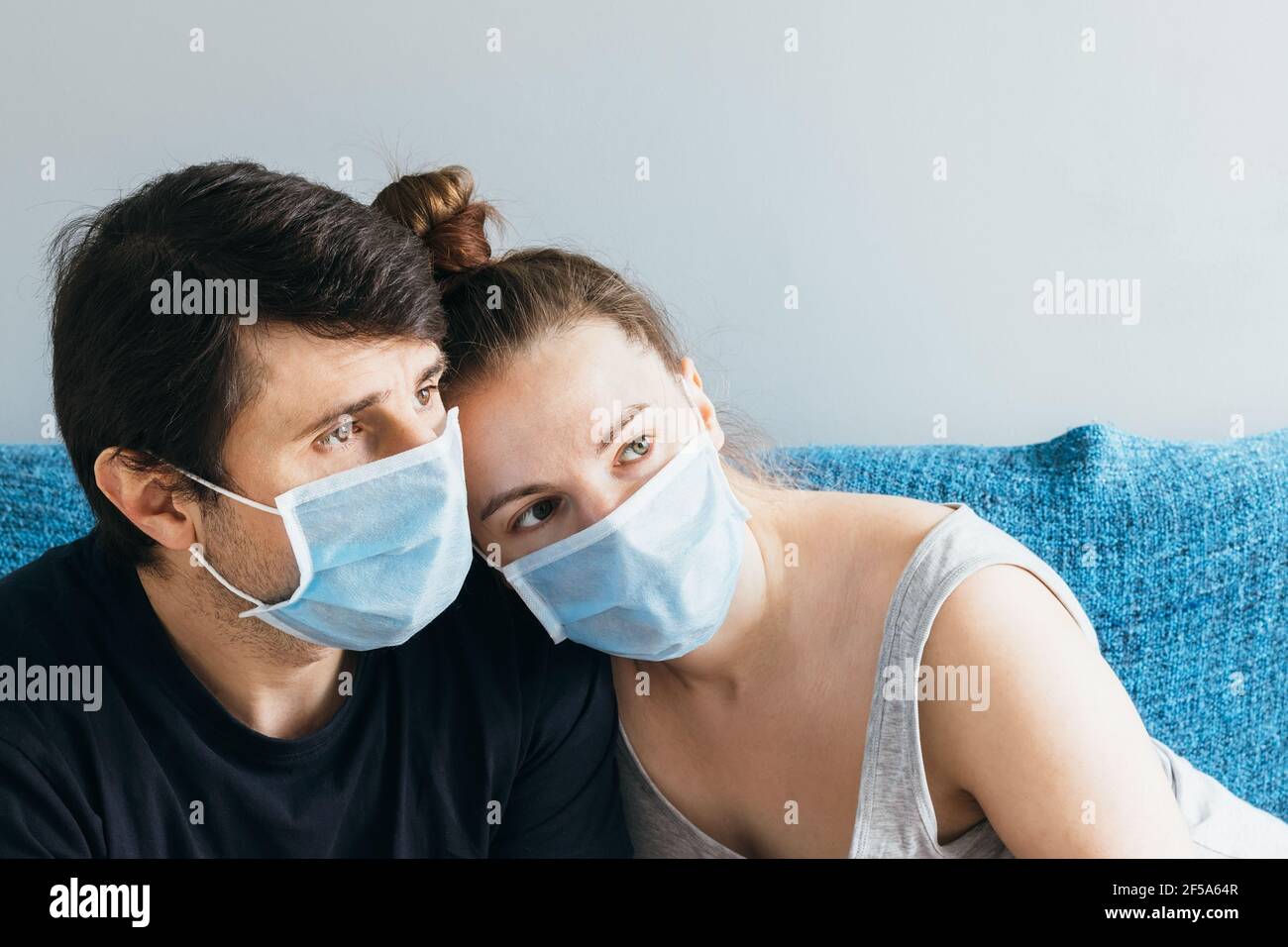 Married couple in blue medical face masks sitting on the couch, hugging ...
