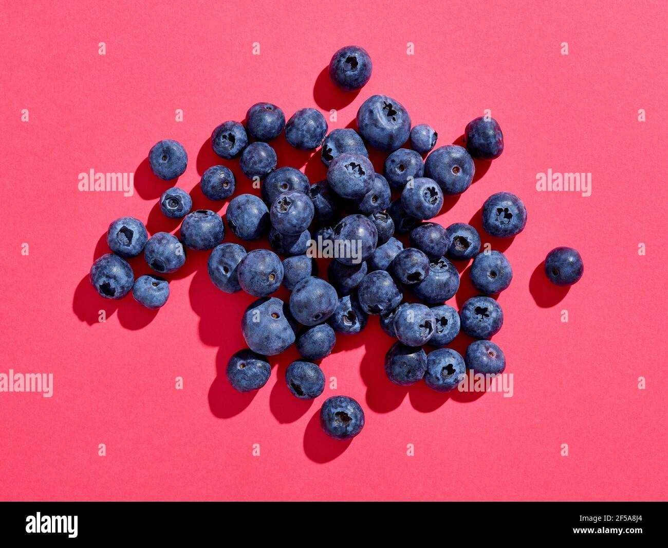Heap of blueberries on pink background; top view; hard dark shadows ...