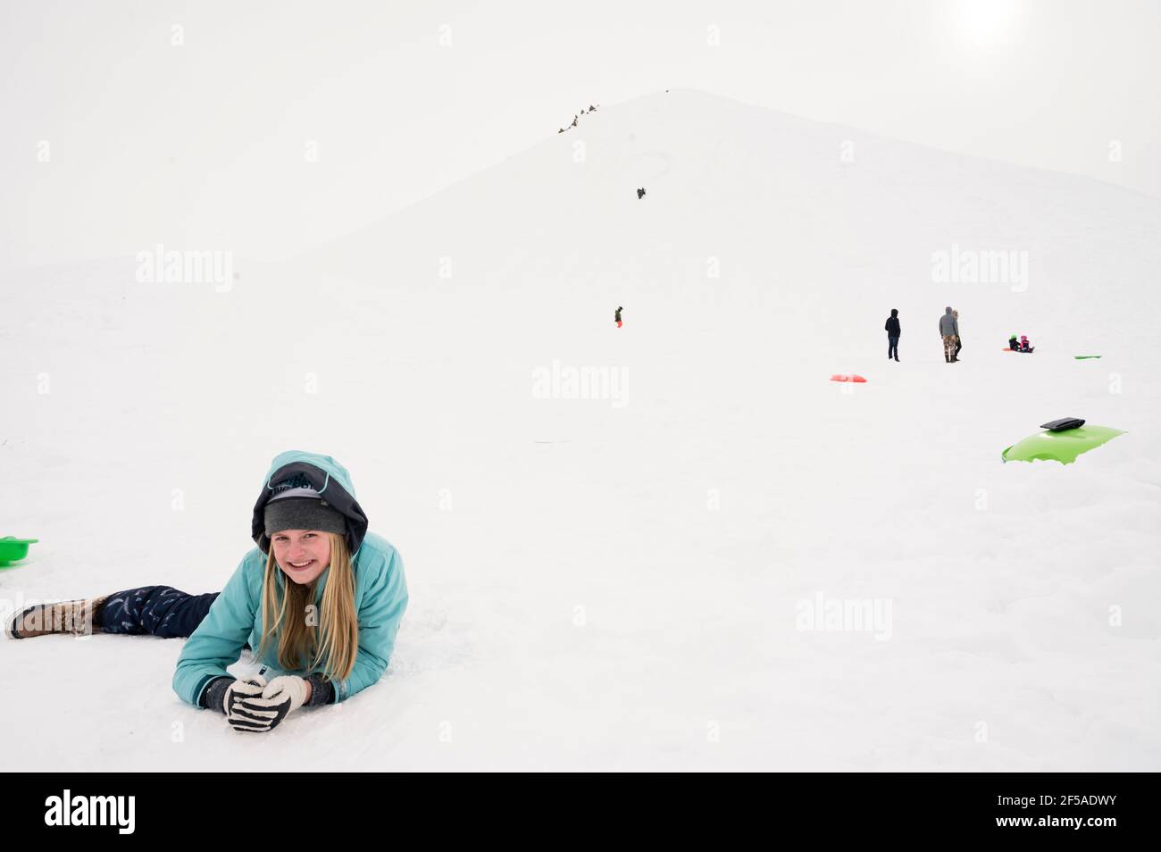 Smiling Young Girl Lying Down at the Bottom of Snowy Sledding Hill ...
