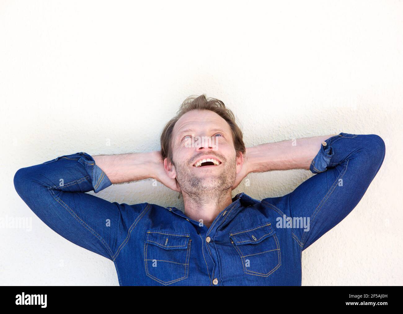 Portrait of handsome man laughing with hands behind head and looking up ...