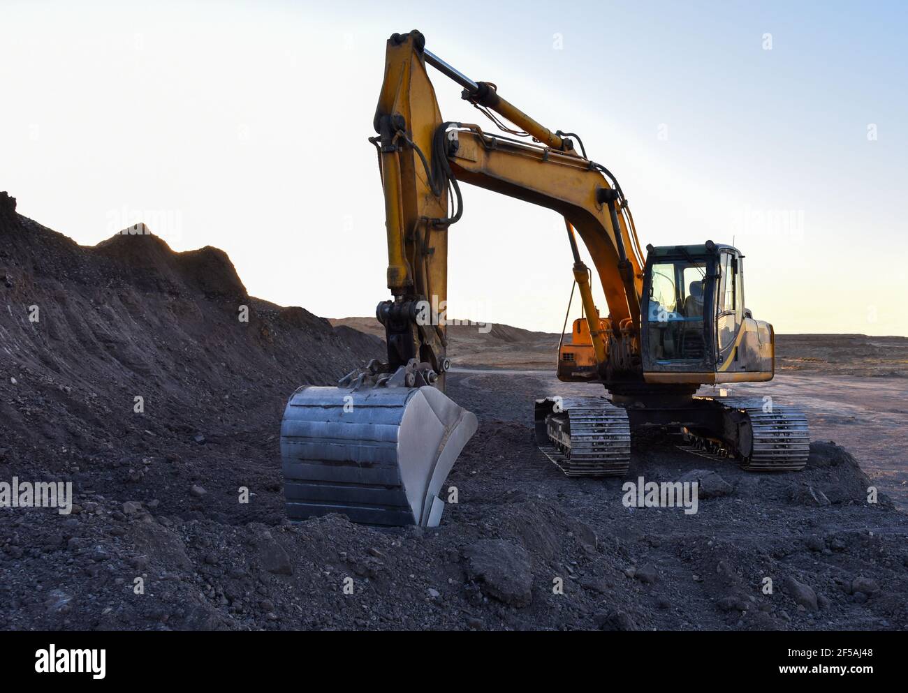 Excavator work at mining quarry on sunset background. Backhoe digs ...