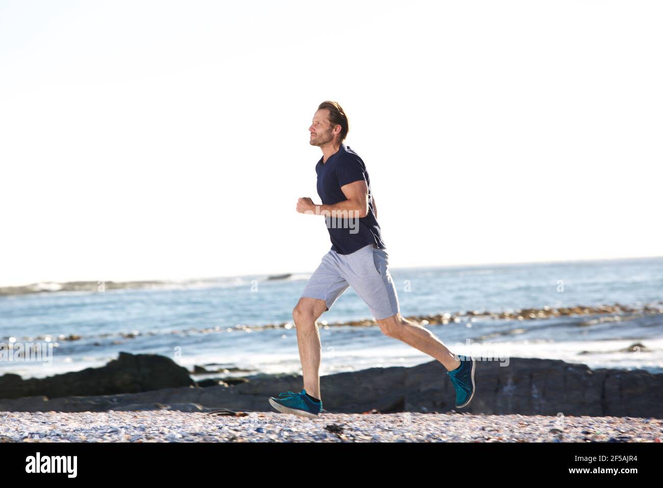 Side full body portrait of active man running by beach Stock Photo - Alamy