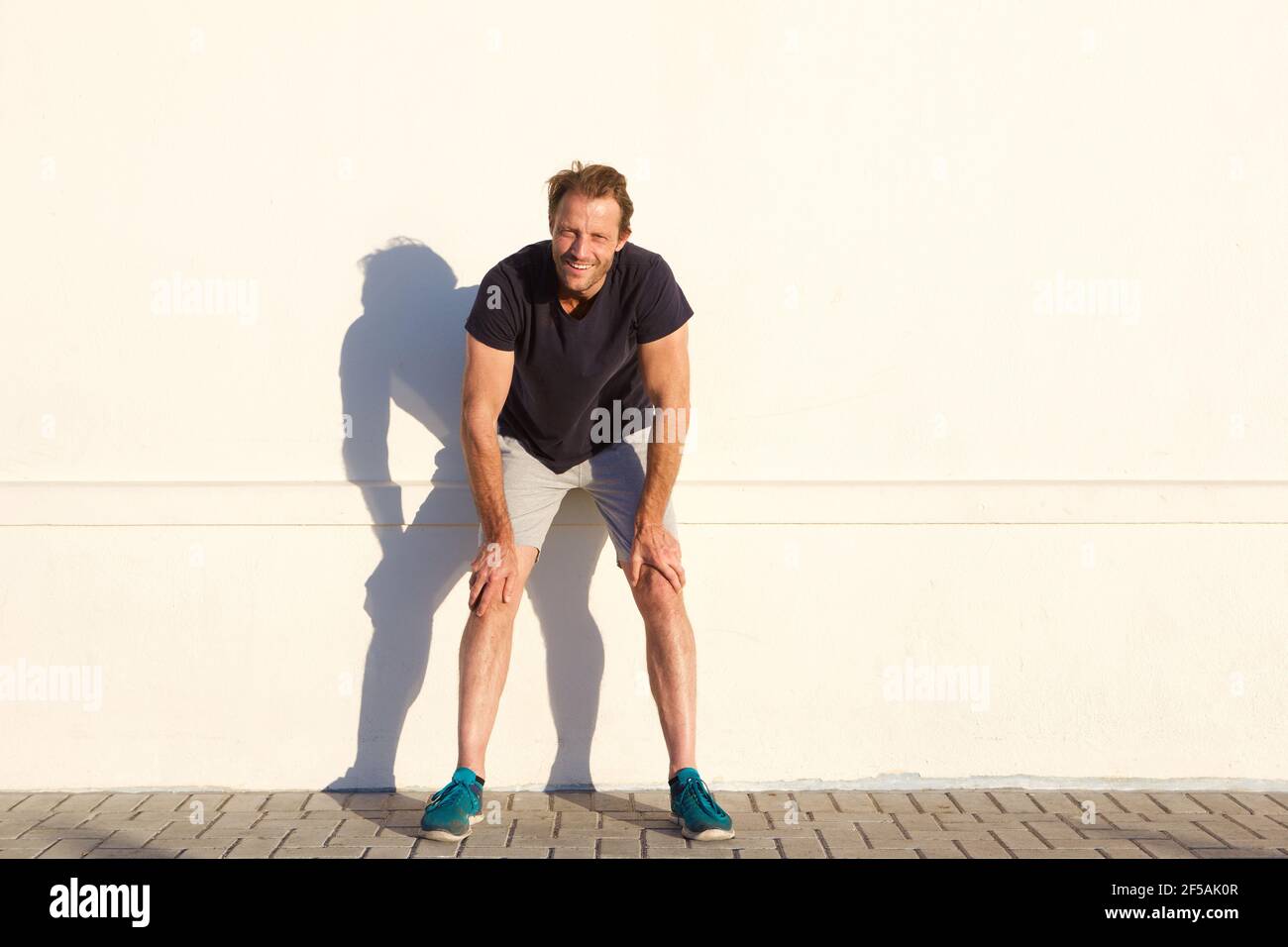 Full length portrait of sports man resting against wall Stock Photo - Alamy