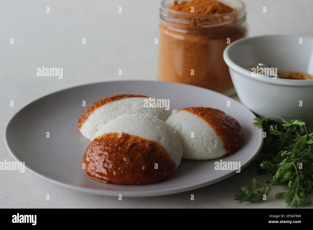 Idli half covered with podi chutney also named gunpowder. Podi is made ...