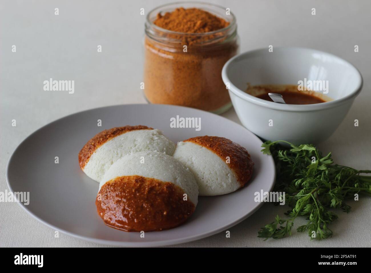 Idli half covered with podi chutney also named gunpowder. Podi is made ...