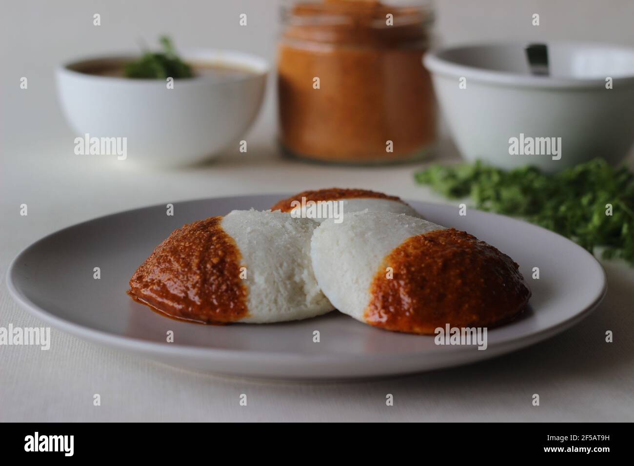 Idli half covered with podi chutney also named gunpowder. Podi is made ...