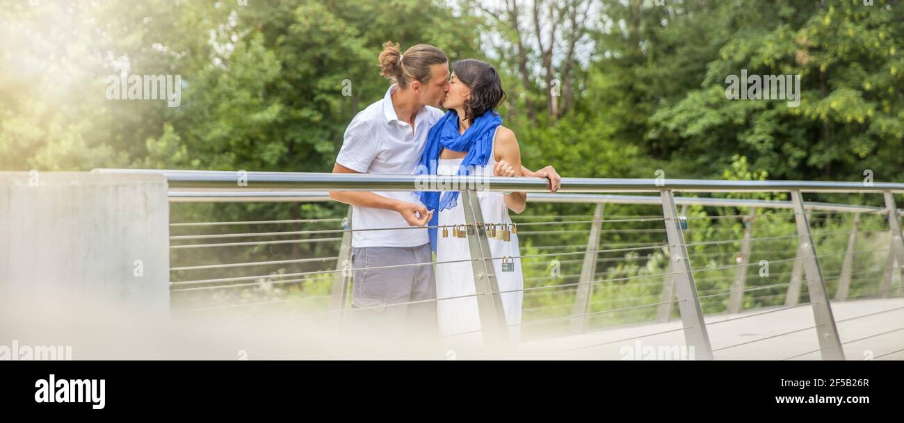 Cute Caucasian couple kissing and hanging a lock on the bridge as a ...