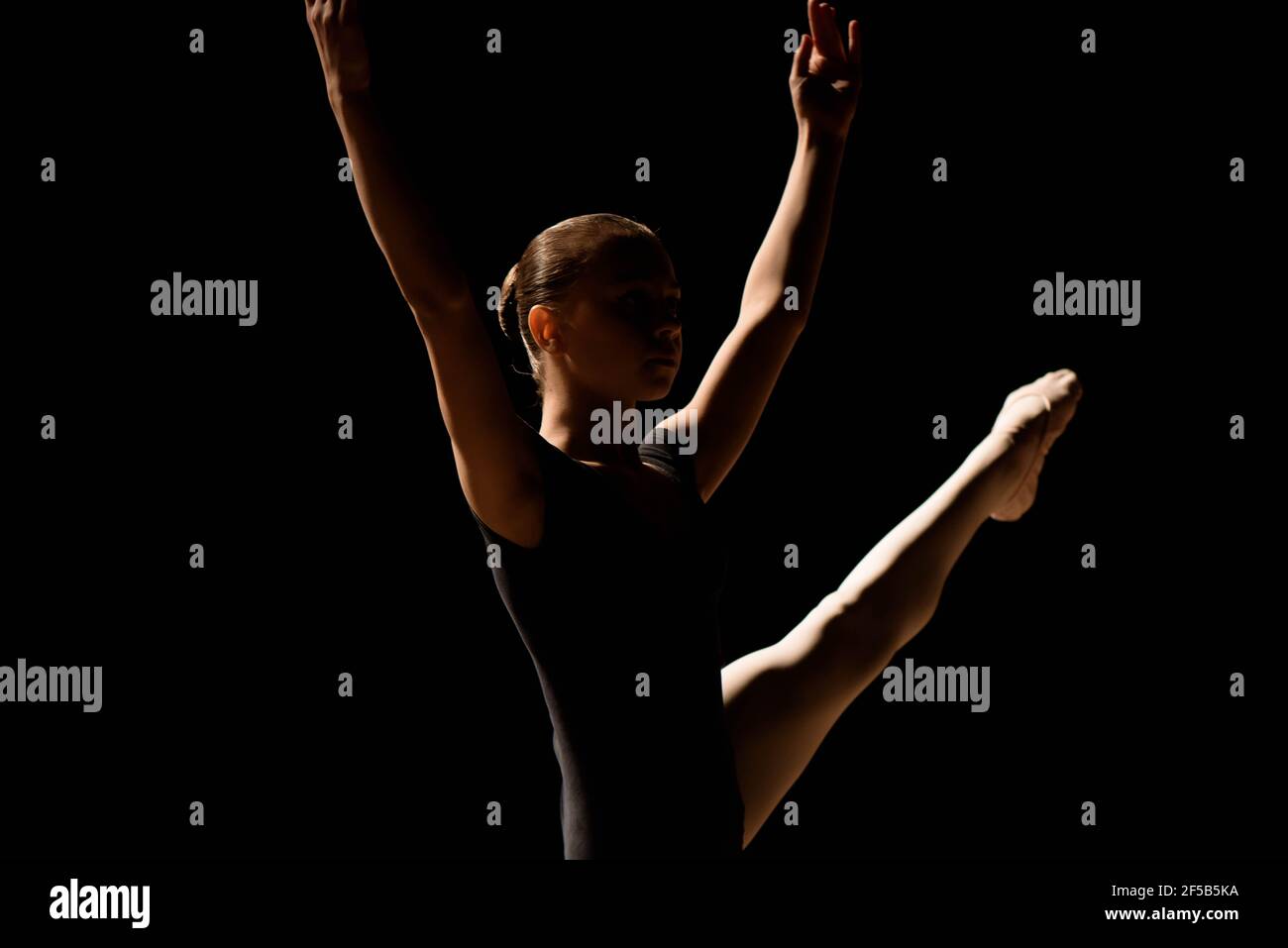 Cute little ballerina in dark ballet costume dancing on the stage. Kid ...