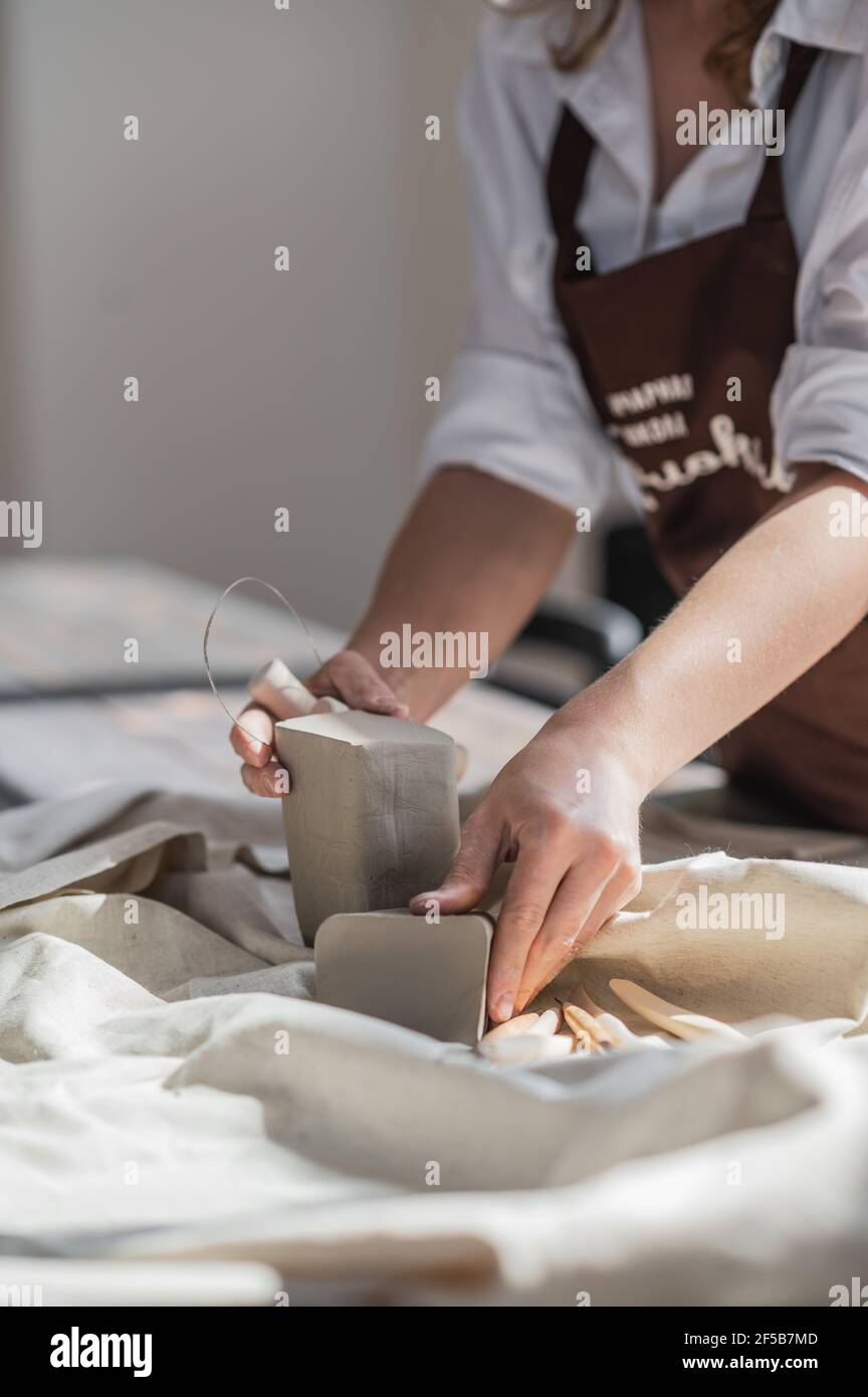 Female potter cutting piece of pottery clay using trimming tool close ...