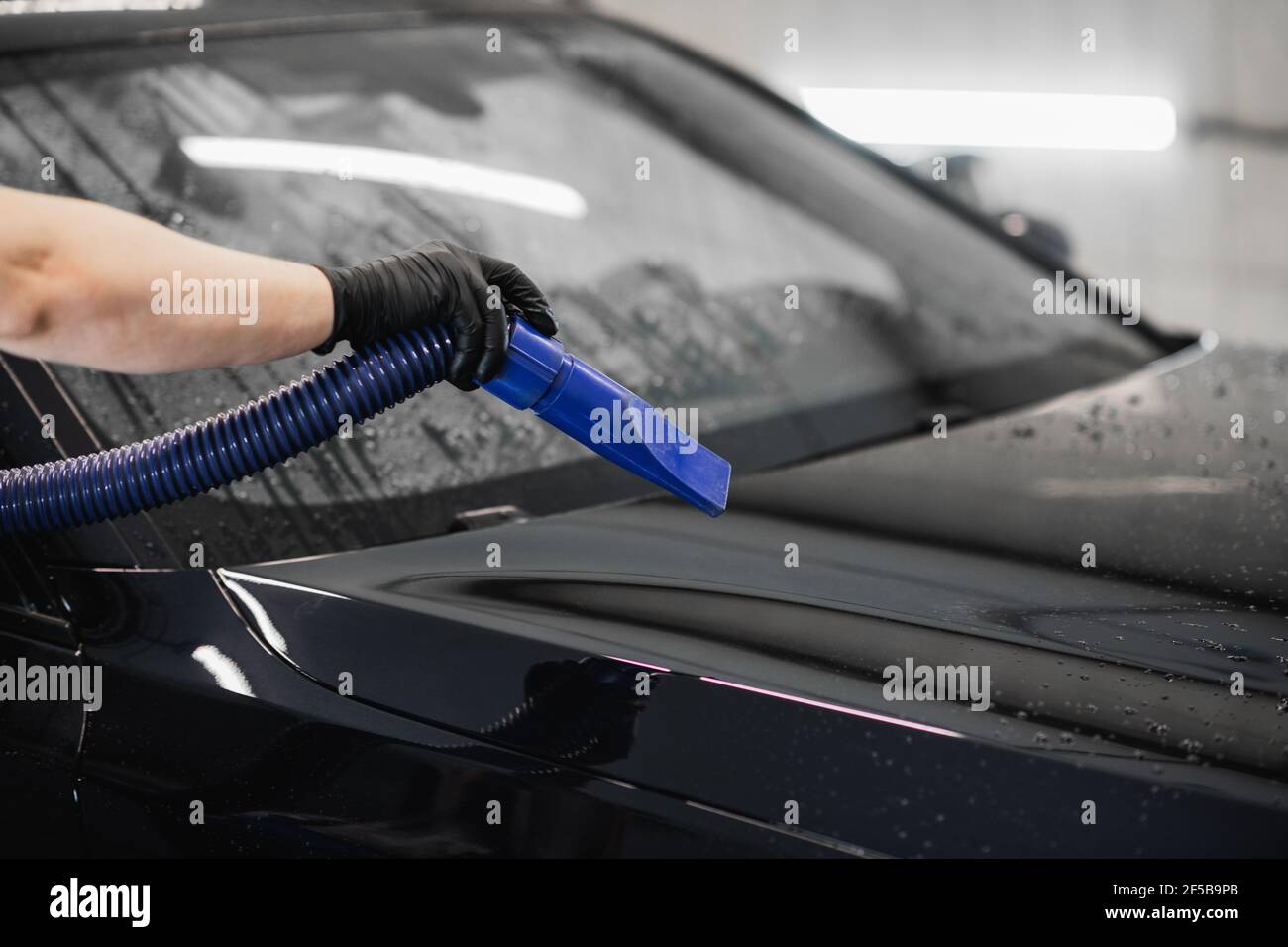 Man blowing off water from freshly washed black car with air. Car wash ...