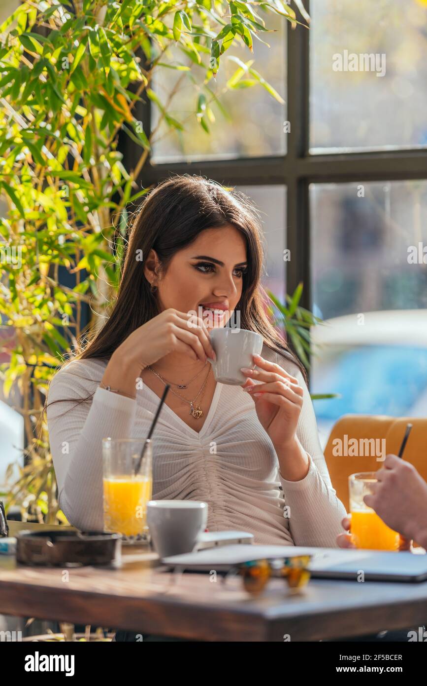 Portrait of a happy young woman drinking coffee while sitting near ...