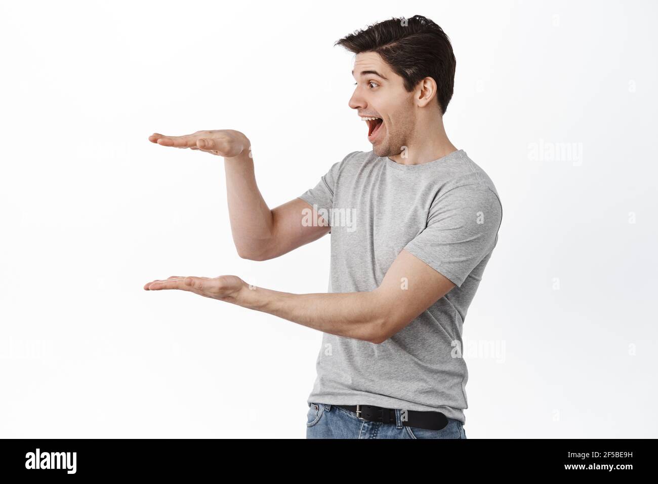Excited and happy young man looking at his hands holding empty copy ...