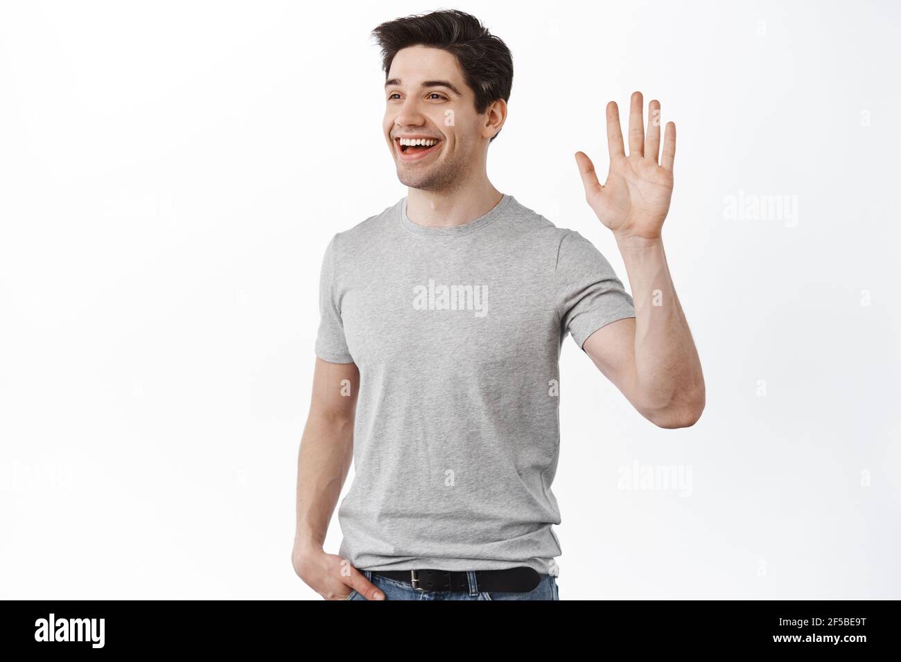 Hello, hey over hear. Smiling handsome man looking and waving aside ...