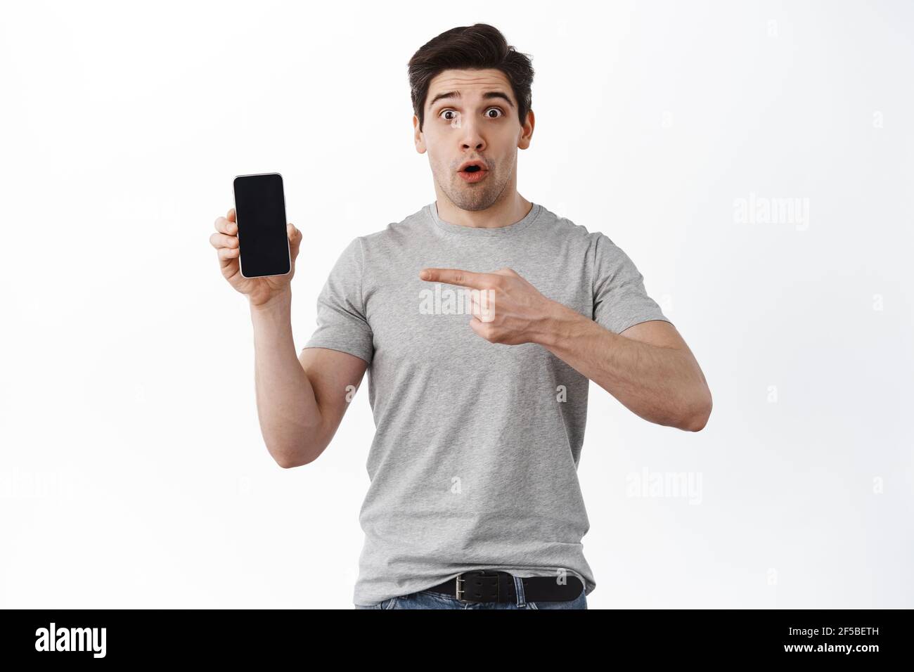 Excited and surprised guy pointing at phone screen, showing cellphone ...