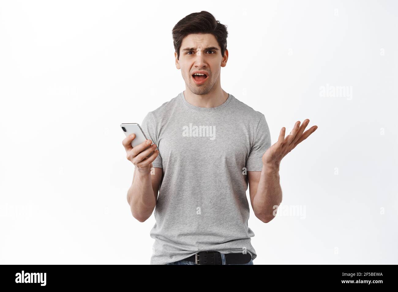 Portrait of confused man with smartphone, holding phone and complaining ...