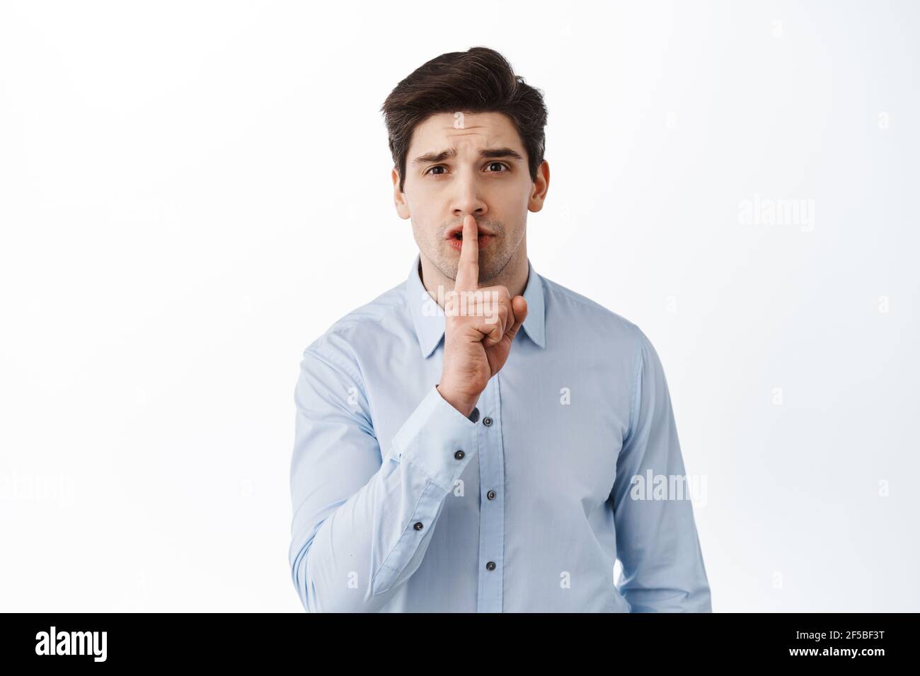Man office worker shushing, asking to keep quiet, press finger to lips ...
