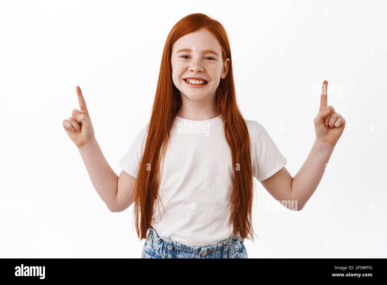 Cheerful redhead girl smiling with teeth and pointing fingers up ...