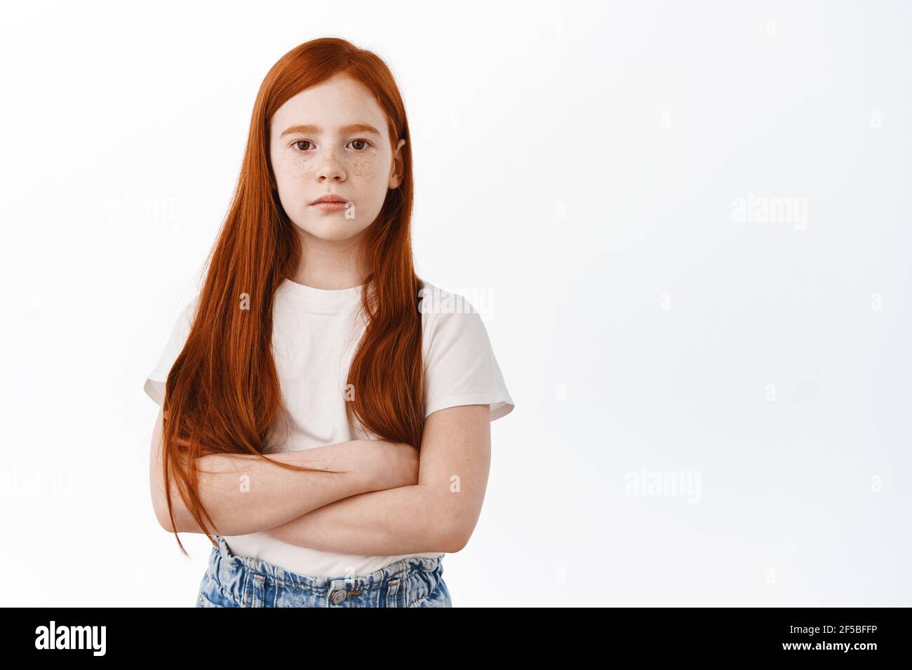 Serious little girl with ginger hair cross arms on chest and look ...