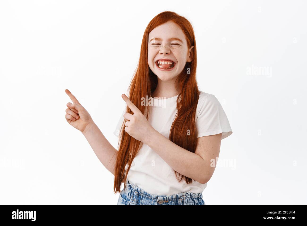 Funny ginger little girl points upper left corner aside, smiles and ...