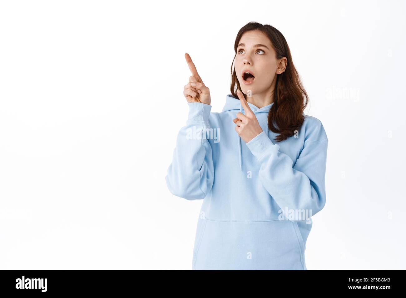 Amazed young woman student gasping, pointing and staring at upper left ...
