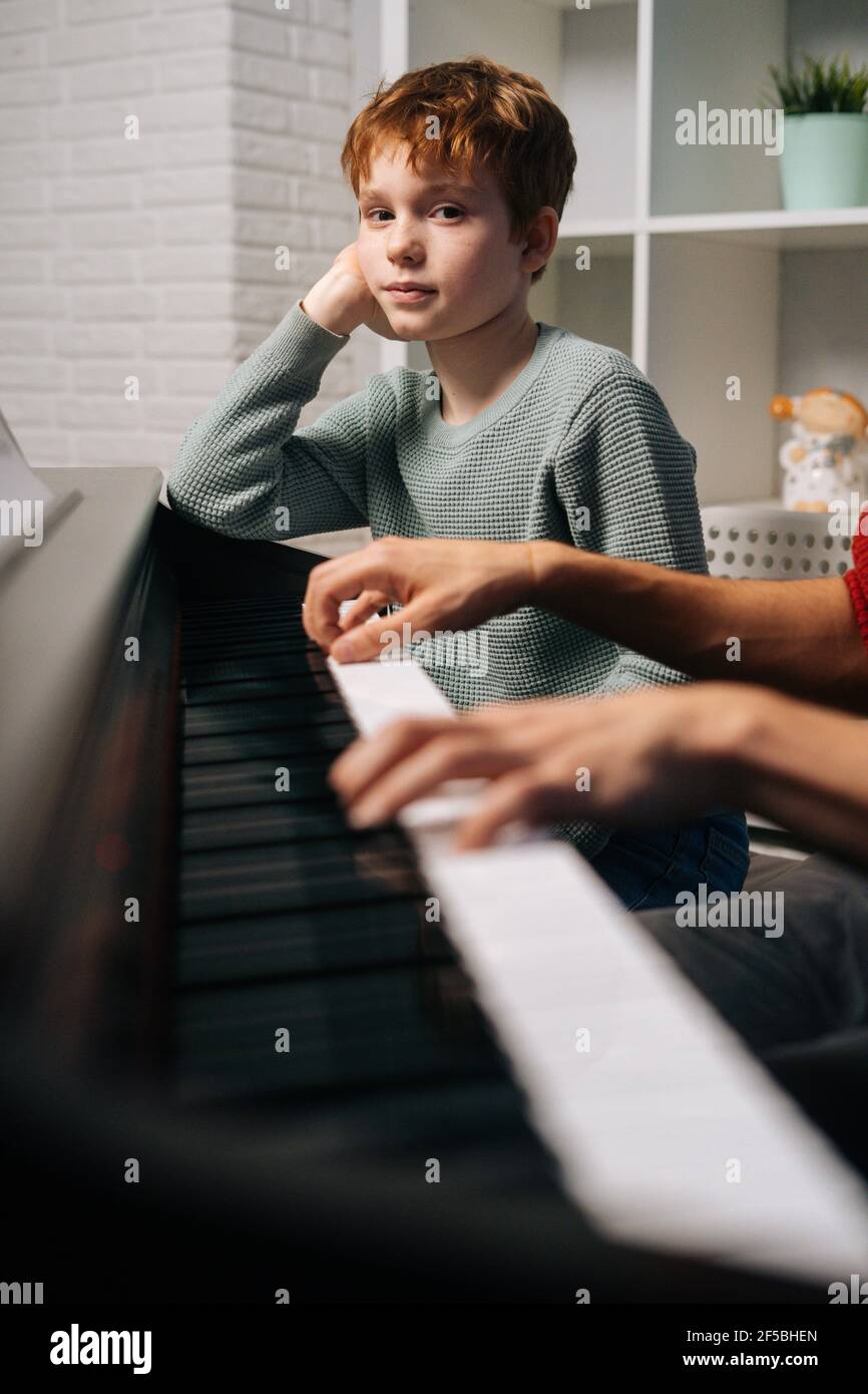 Focused redhead child student boy listening his teacher play the piano ...