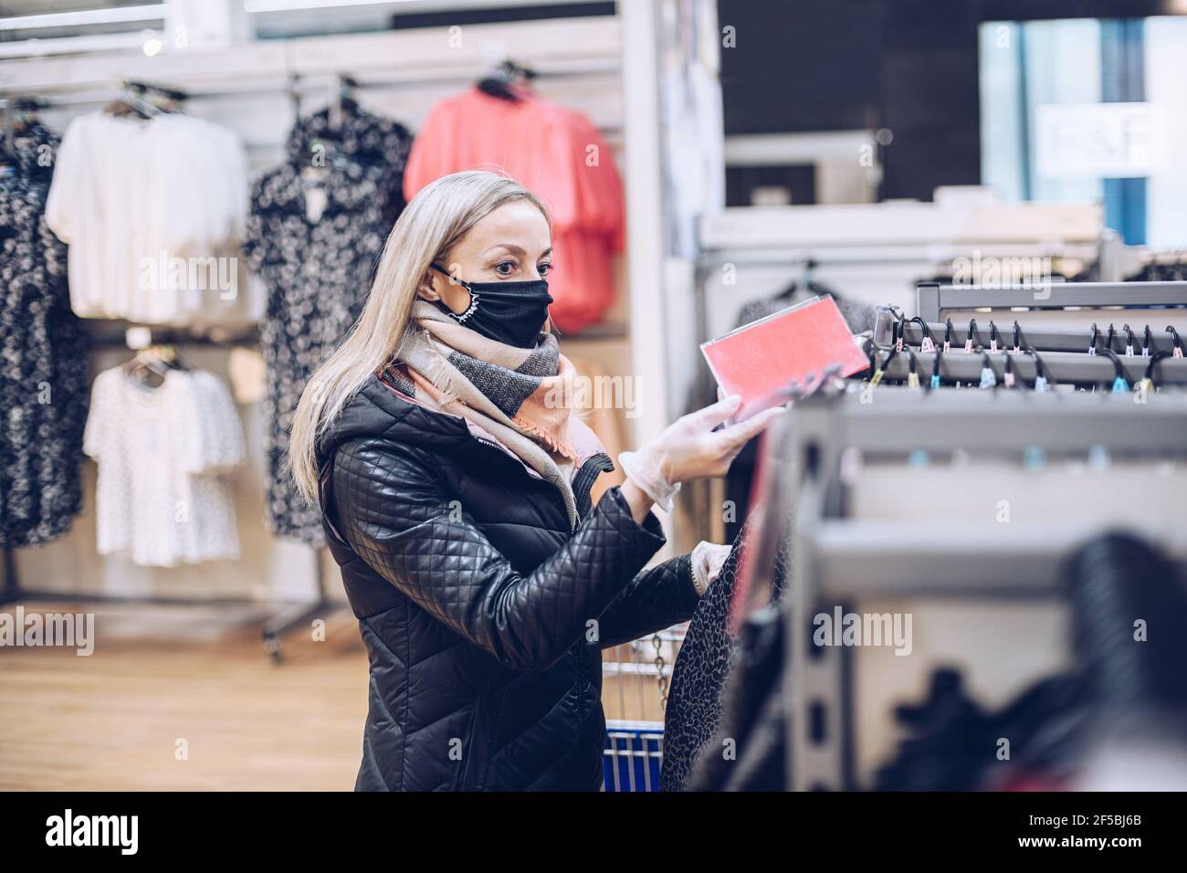 Blonde woman wearing a face mask while shopping in a clothing ...