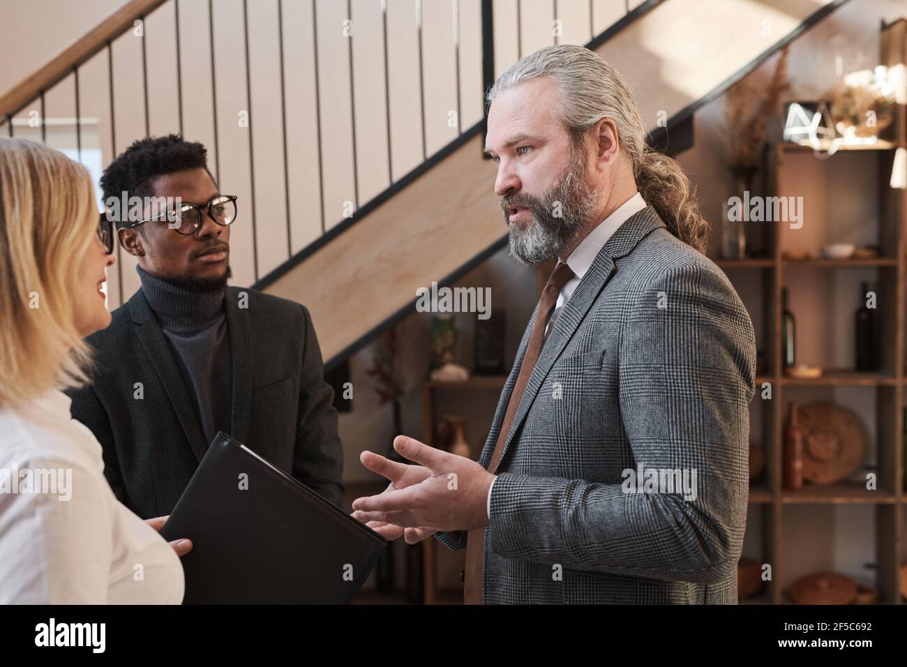 Mature businessman in suit giving instructions to his employees before ...