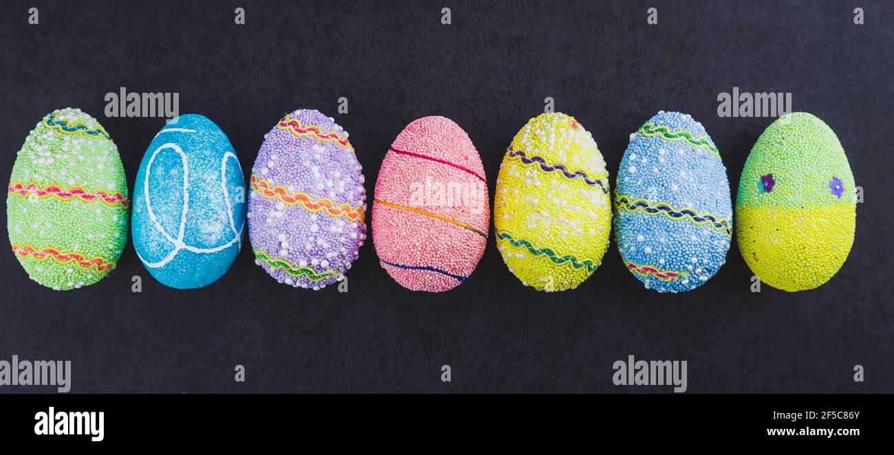 Colorful Easter eggs lined up side by side on a trendy black background ...