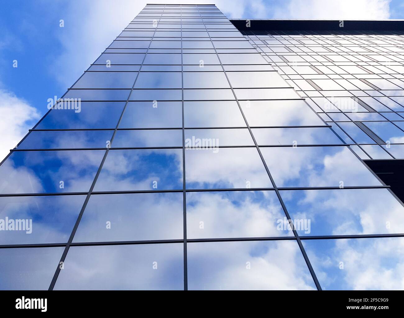 View of a modern glass skyscraper. Reflection of a cloudy blue sky in a ...