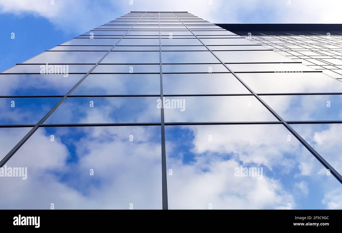 View of a modern glass skyscraper. Reflection of a cloudy blue sky in a ...